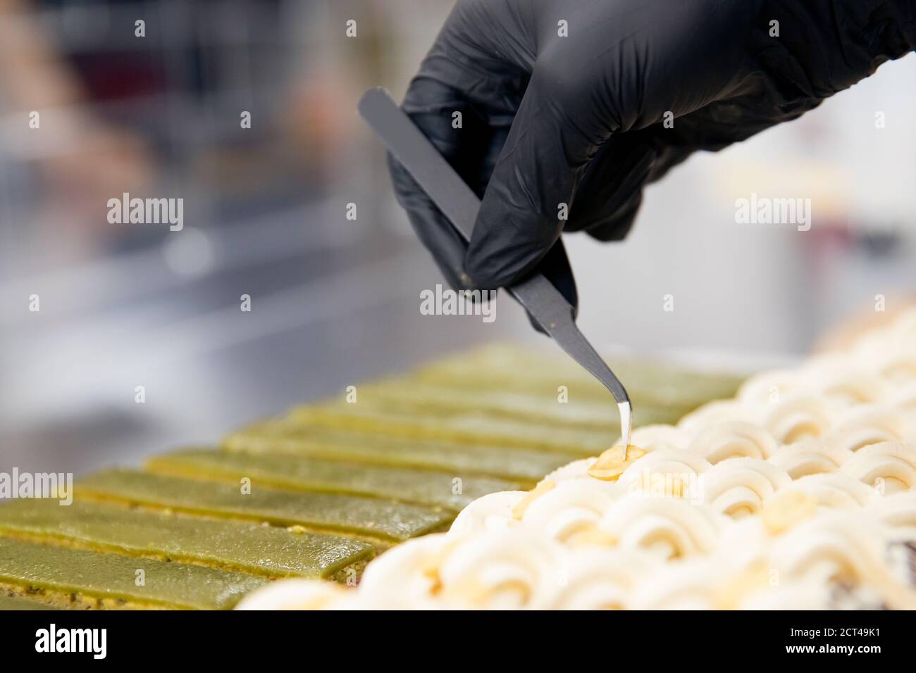 Pastry chef holds tweezers with nuts, decorates cakes before serving in ...