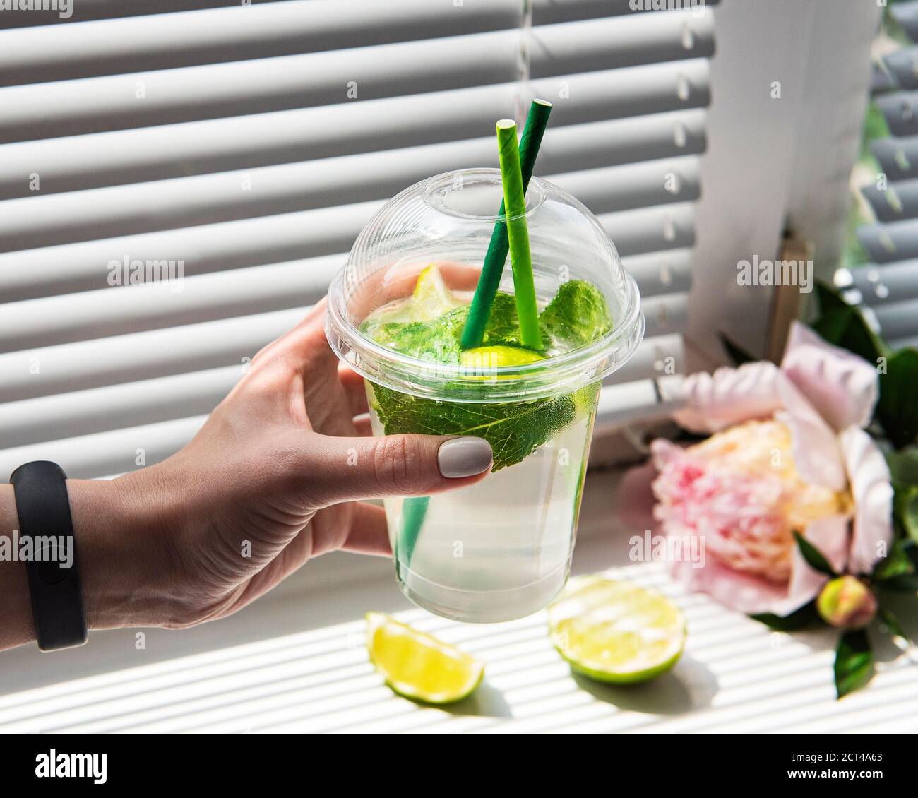 Mojito cocktail in female hands in front of the window and a bouquet of ...