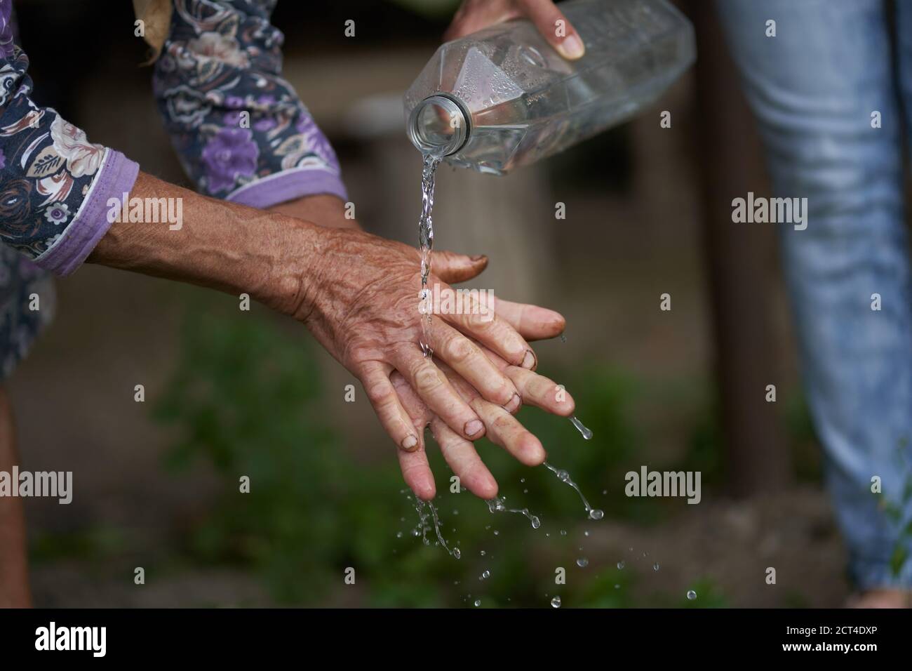 Old woman farmer washing her hands outdoor with water from a plastic ...