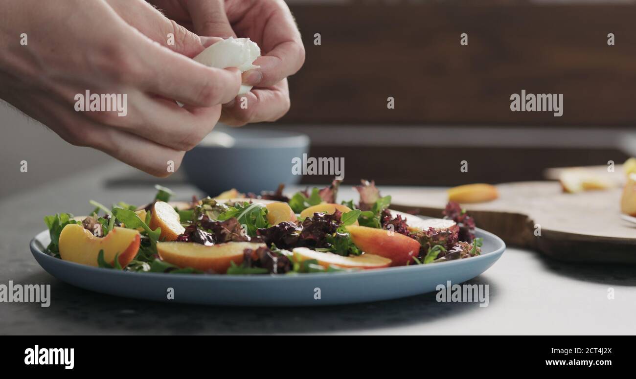 man making salad with nectarines and mozzarella on a blue plate on ...