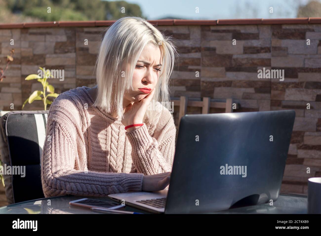 Boring young woman sitting on terrace while using a laptop Stock Photo ...