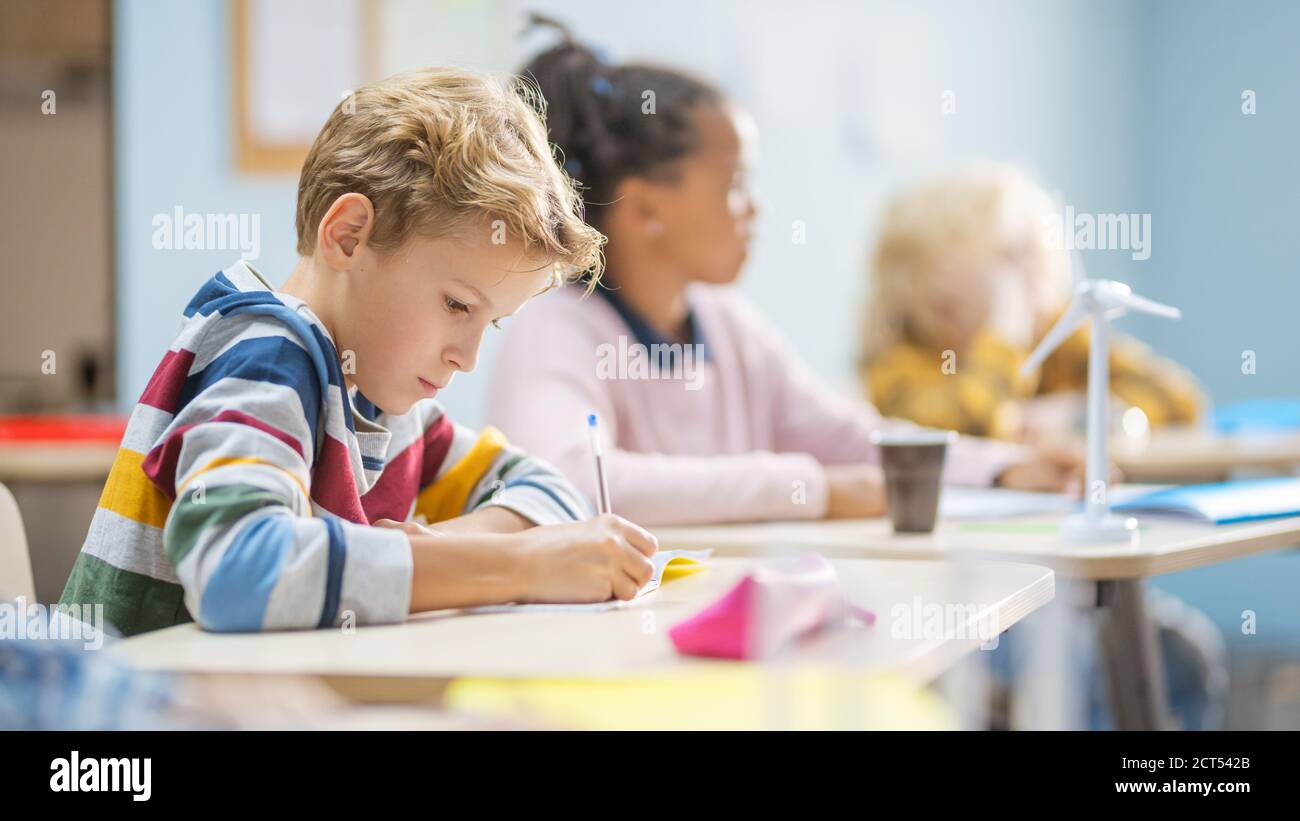 In Elementary School Classroom Brilliant Caucasian Boy Writes in ...