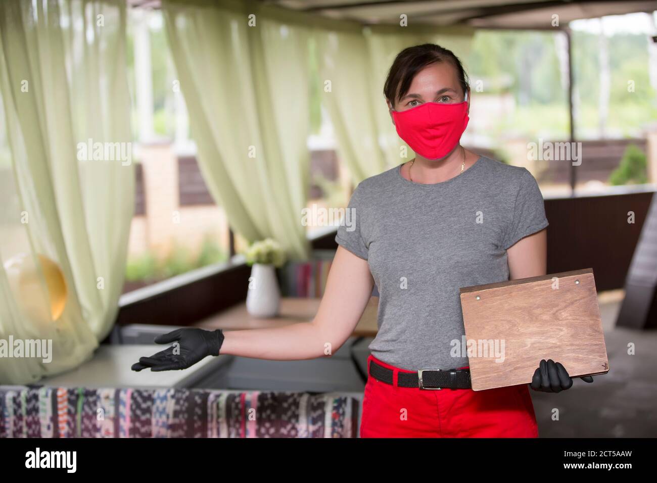 Happy waiter with protective mask holds the menu and invites to the ...