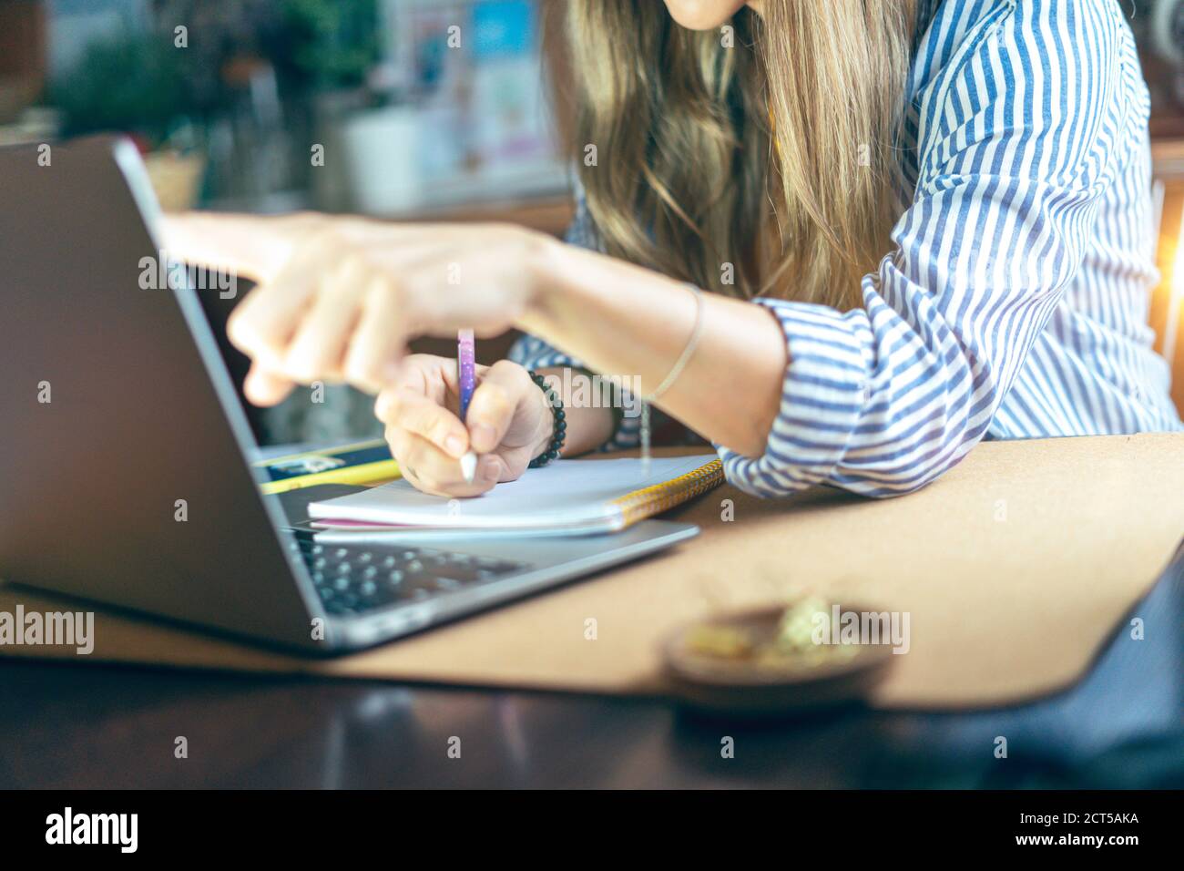Business woman writes in notebook on desk and pointing hand at computer ...