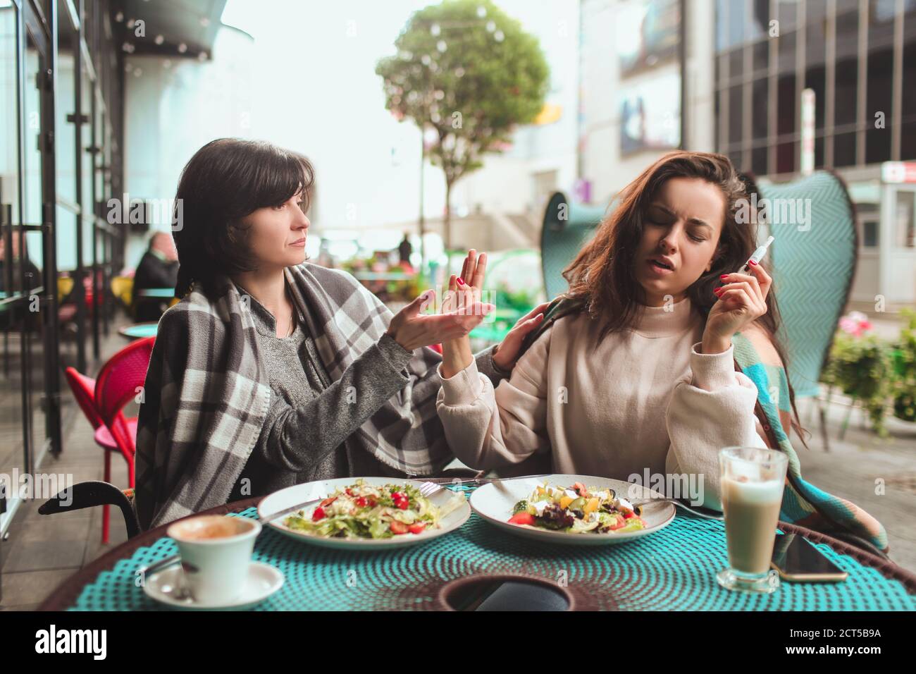 Mature mother and her young daughter sit together in cafe or restaurant. Girl smoking electronic ...