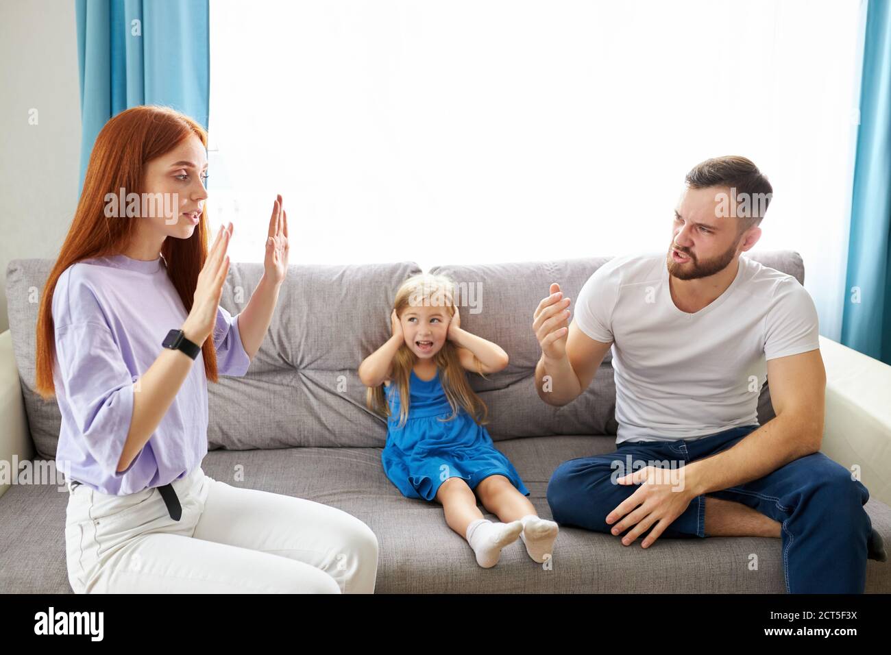 sad, desperate little girl during parents quarrel, she clog the ears sitting on sofa at home ...