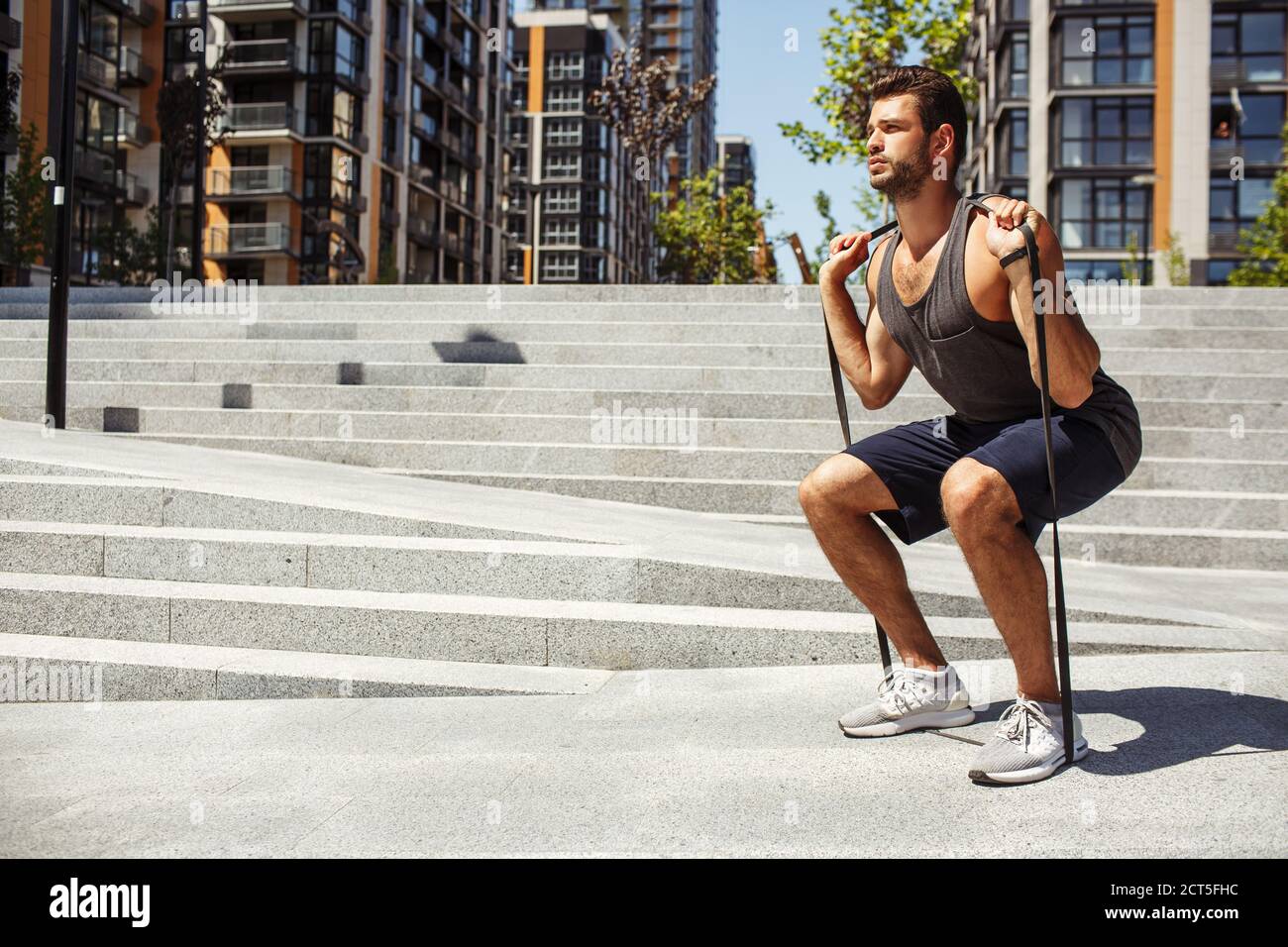 Young man exercising outside. Guy holding rubber band on shoulders and ...