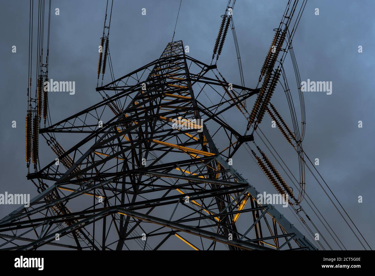 Looking up at sunlit electricity pylon with moody sky at dusk before a ...