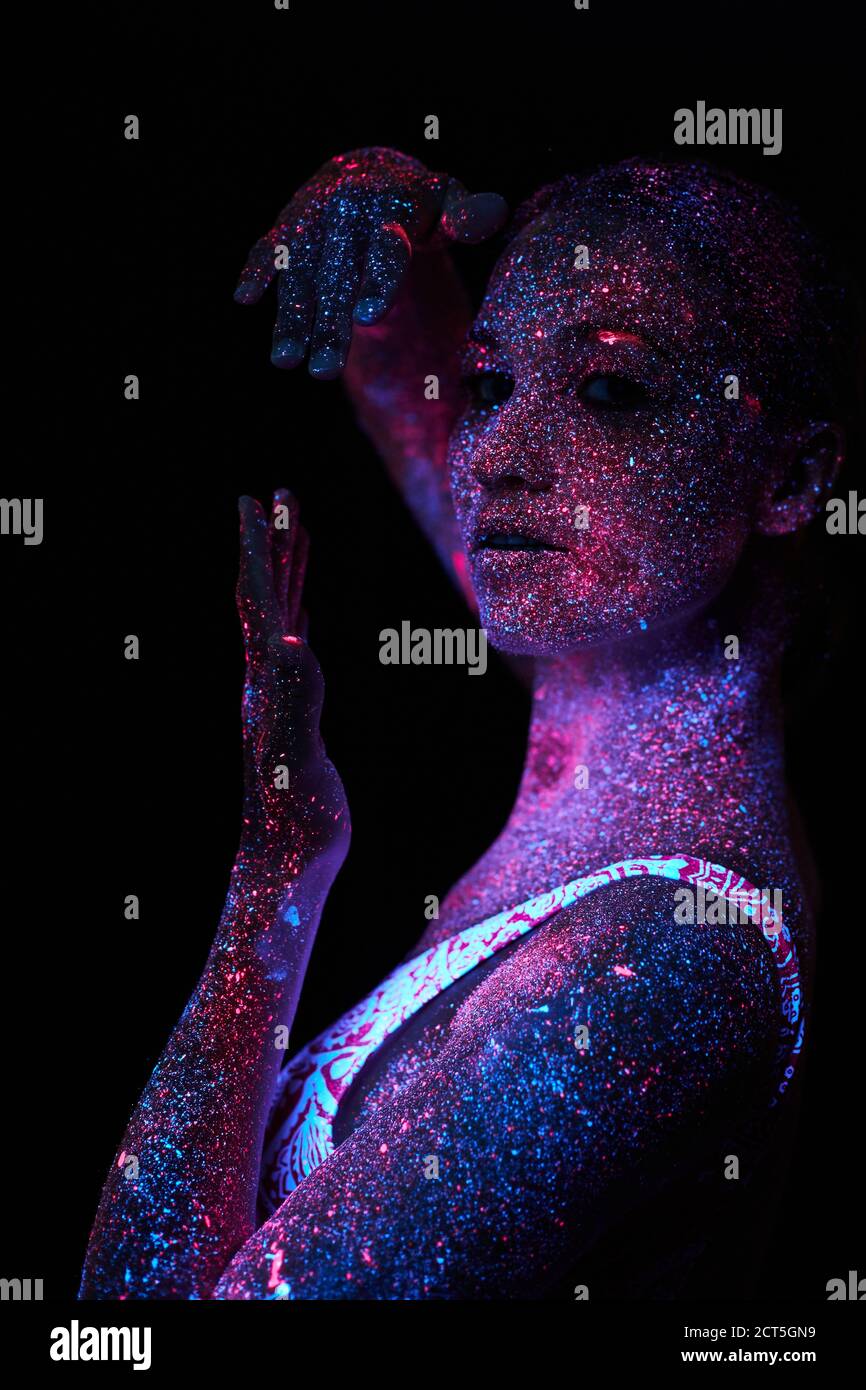 Art woman cosmos in ultraviolet light. Entire body is covered with colored droplets. Girl posing ...