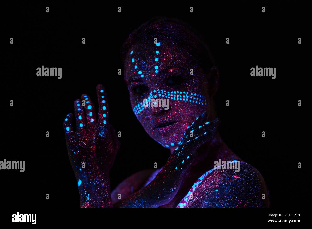 Art woman cosmos in ultraviolet light. Entire body is covered with colored droplets. Girl posing ...