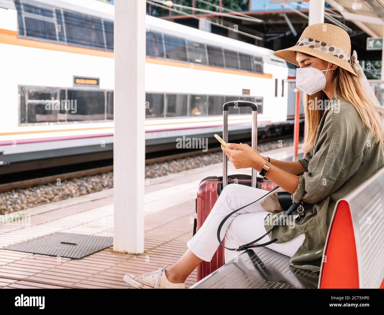 Side view of young woman in protective mask sitting on bench on ...