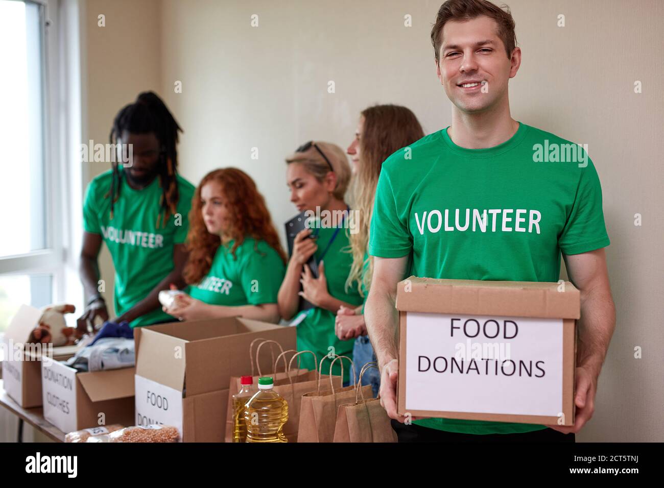 portrait of affable volunteer man in green t-shirt holding donation box ...
