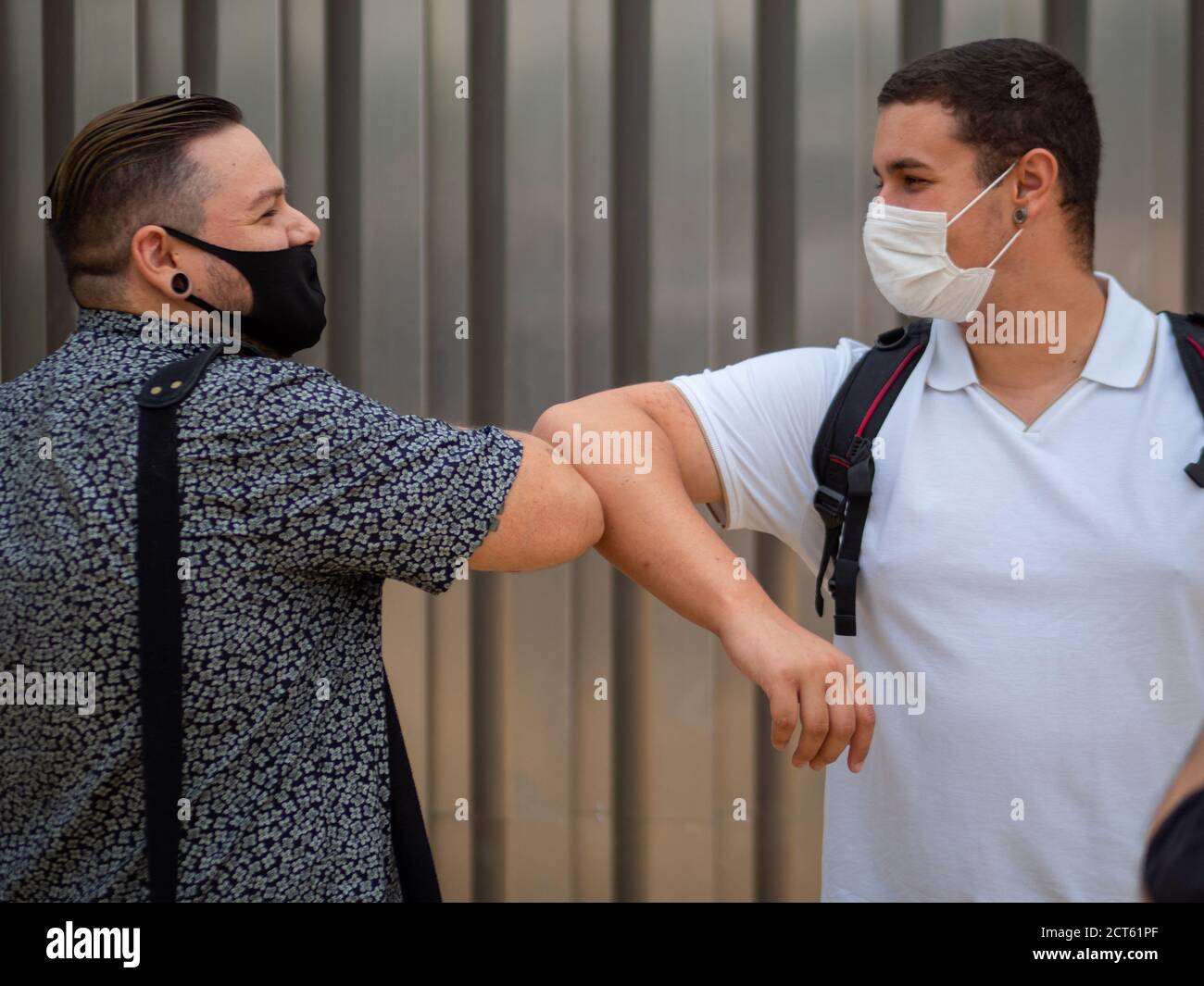 Shot of two young men wearing medical masks greeting each other by arms ...