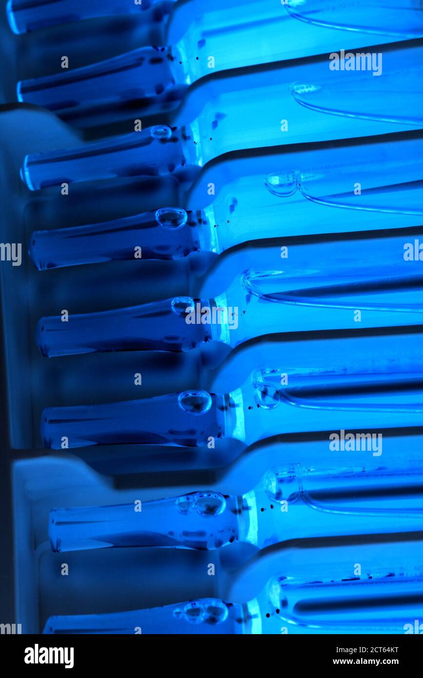 Closeup of row of upright ampules in ultra violet lighting with ...