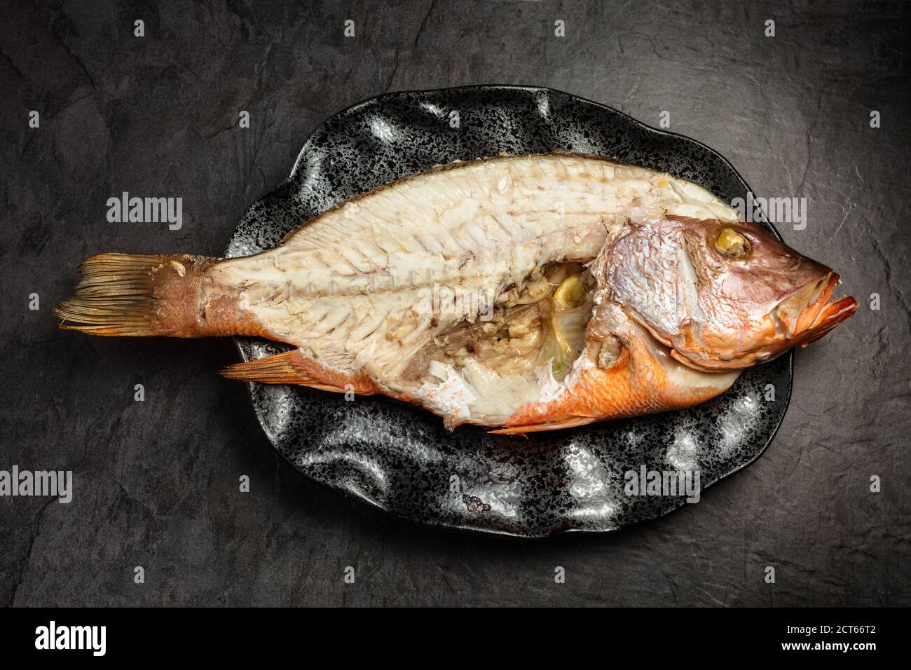 Half eating red snapper fish with exposed bones, on dark background ...