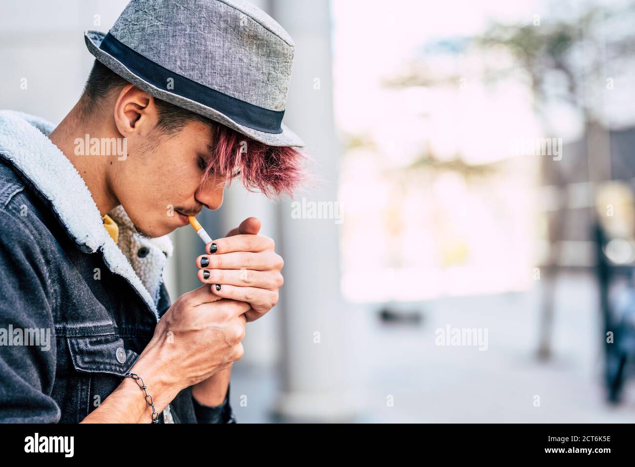 Young modern caucasian teenager male with violet hair and hat light a ...