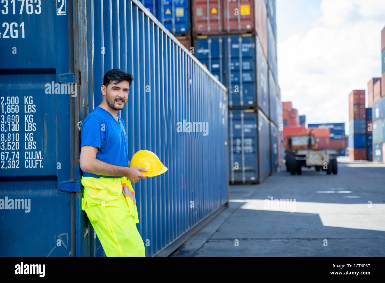 Portrait of container worker leaning on cargo container and looking up ...