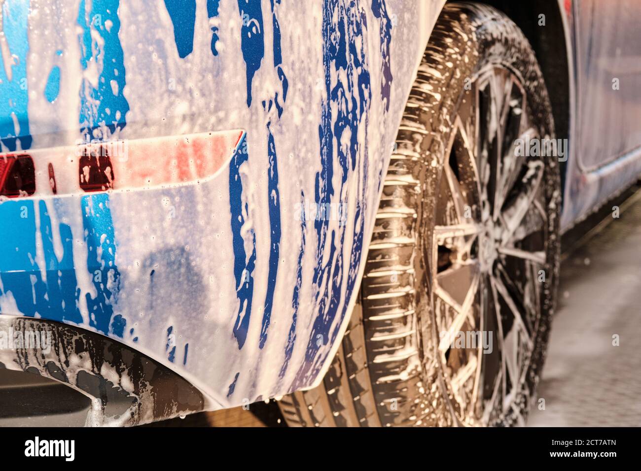 Close up a wheel of a blue car washing under high pressure with foam ...
