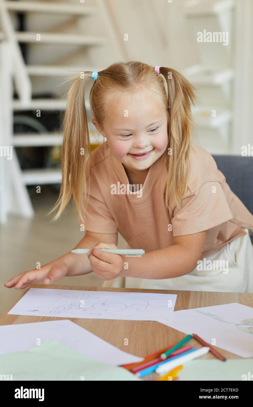 Vertical portrait of cute blonde girl with down syndrome drawing and ...
