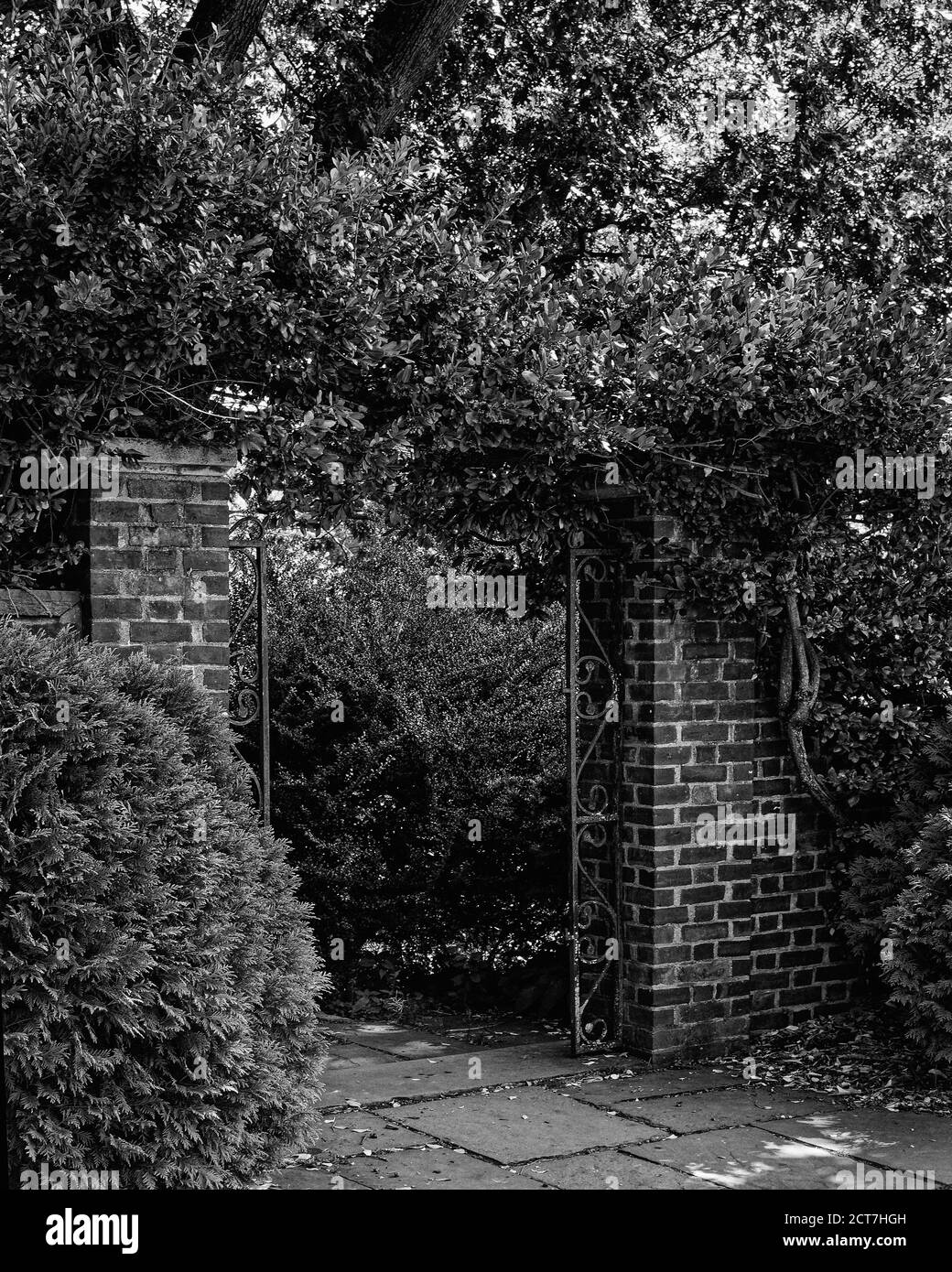 Brick and iron gate open to sunken garden on a sunny summer morning. A ...