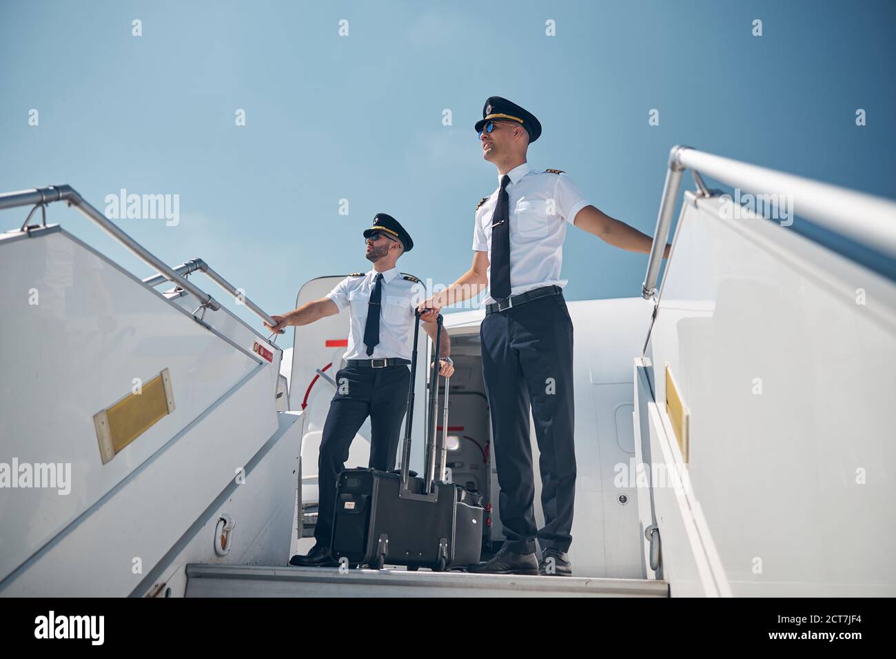 Two senior handsome pilot with rolling bag going home after long flight ...