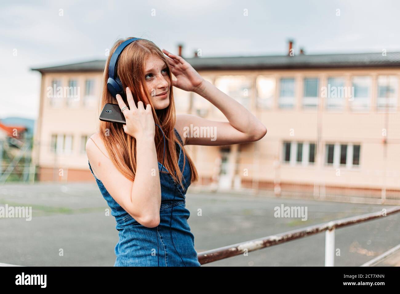 Cute, ginger girl streaming music on her phone. Headphones on her head ...