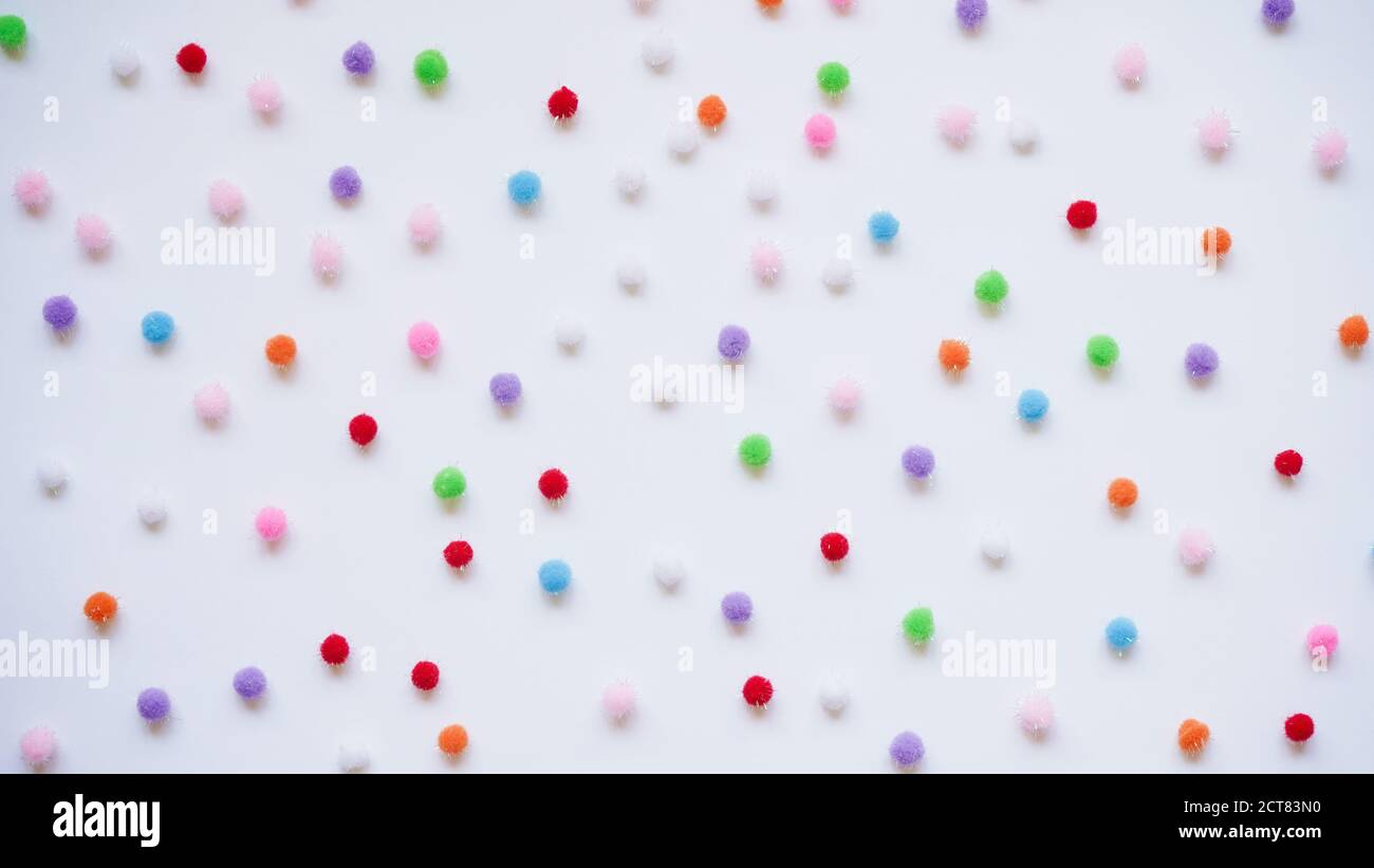 Many small bright colored pom-poms on a white background, top view ...
