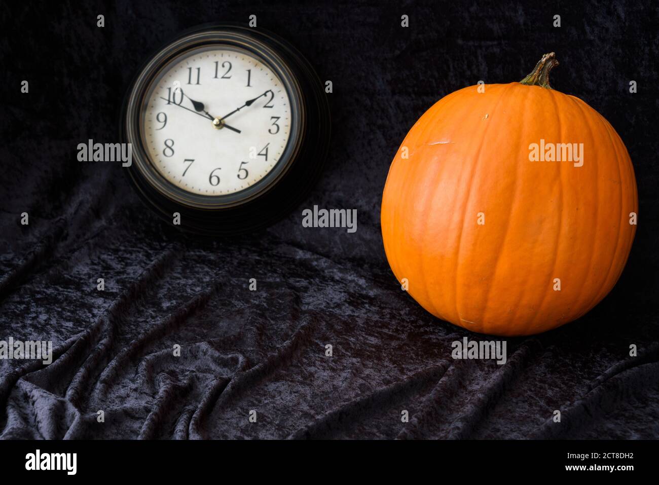 Orange pumpkin and traditional clock on a black velvet background, fall ...