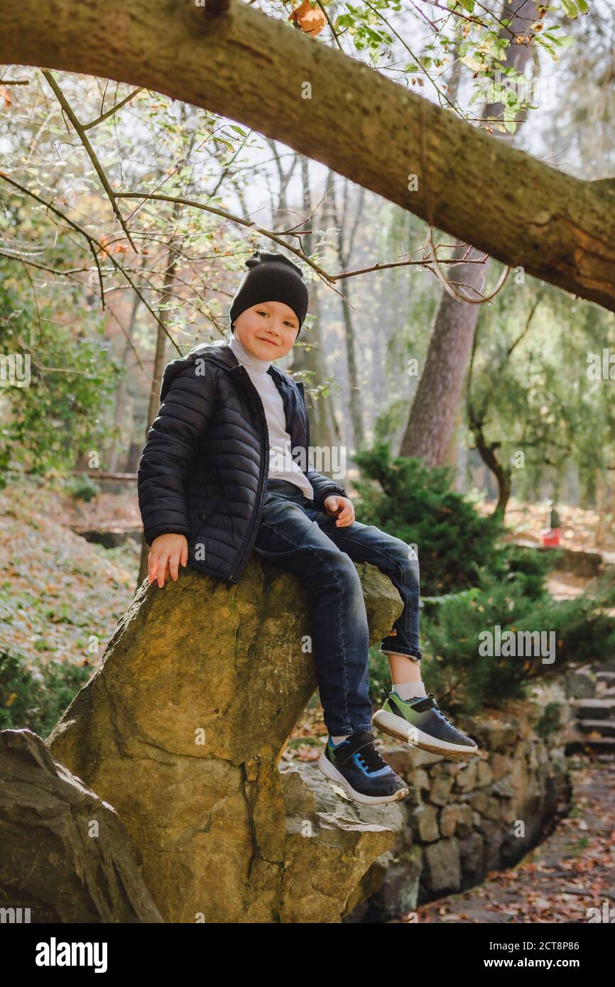toddler boy sitting on the rock at autumn city park Stock Photo - Alamy