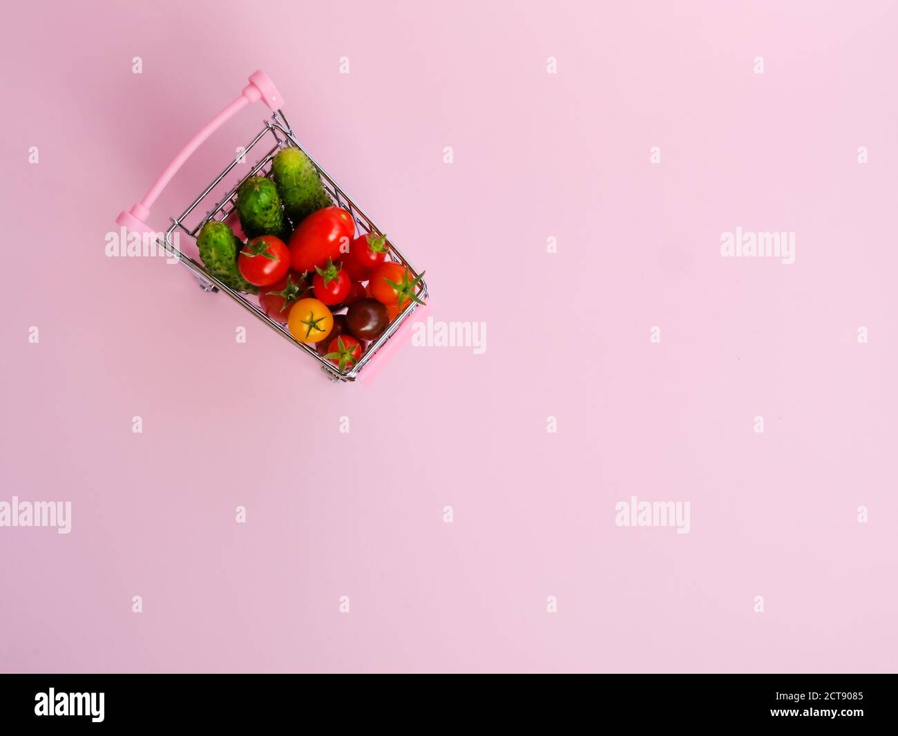 Pink grocery cart full of tomatoes and cucumbers on pink background ...