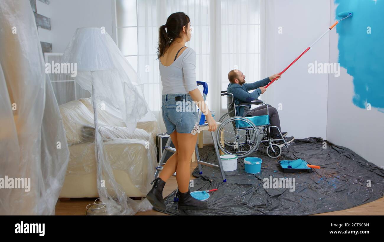 Invalid man painting wall while sitting in wheelchair. Handicapped ...