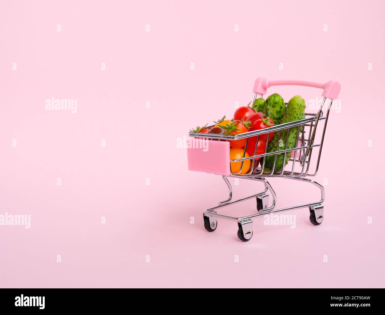 Pink grocery cart full of tomatoes and cucumbers on pink background ...