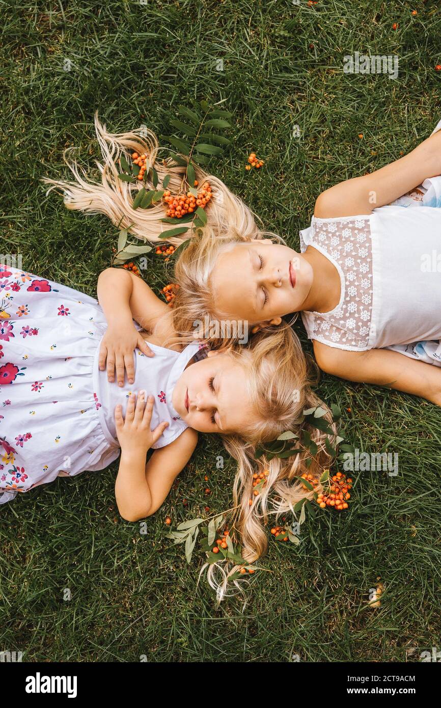 Two little sisters lying on grass, rowan in hair. Eyes closed, serious faces Stock Photo - Alamy