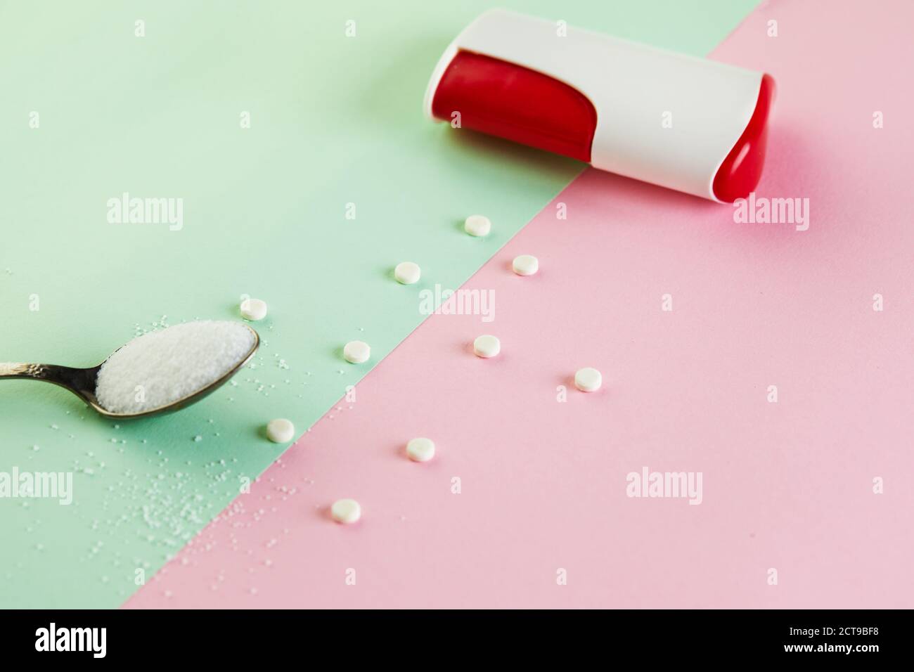 Sugar substitute tablets and natural sweetener powder on a green-pink ...