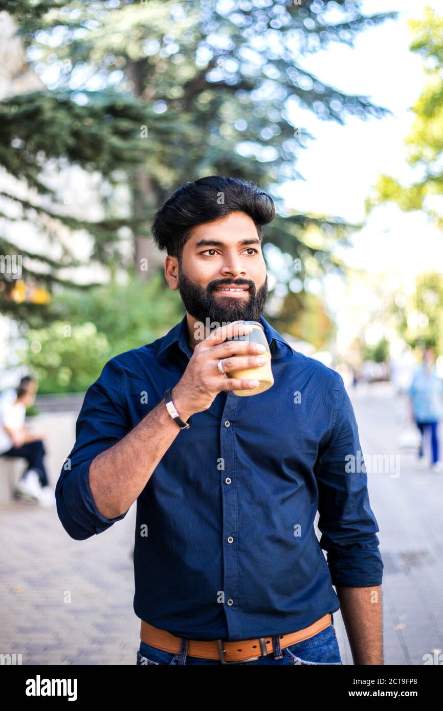 Young Indian man drinking coffee from reusable cup outdoors Stock Photo ...