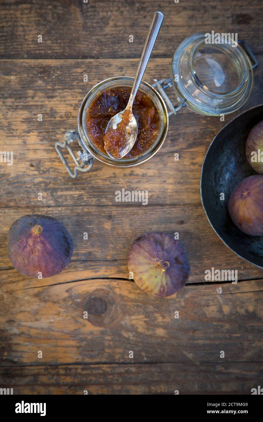 Four figs (Ficus carica) and a glass of fig jam on wooden table, studio ...