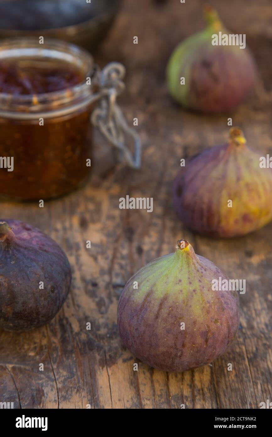 Four figs (Ficus carica) and a glass of fig jam on wooden table, studio ...