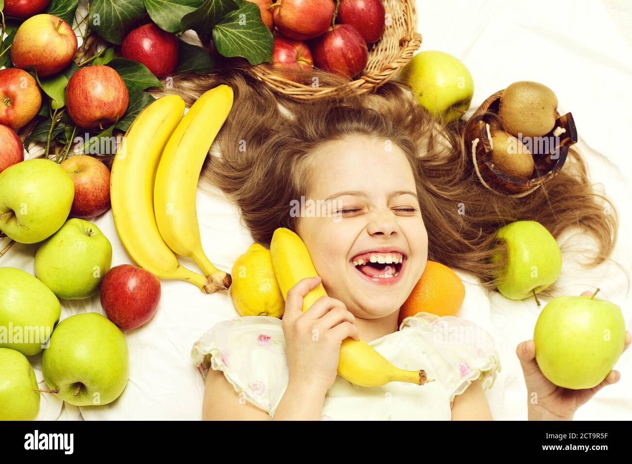 child or cute baby girl laying with colorful fruits hold banana as ...