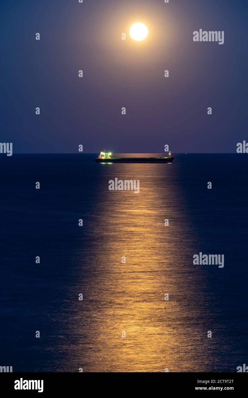 Cargo ship at night with full moon over the horizon Stock Photo - Alamy