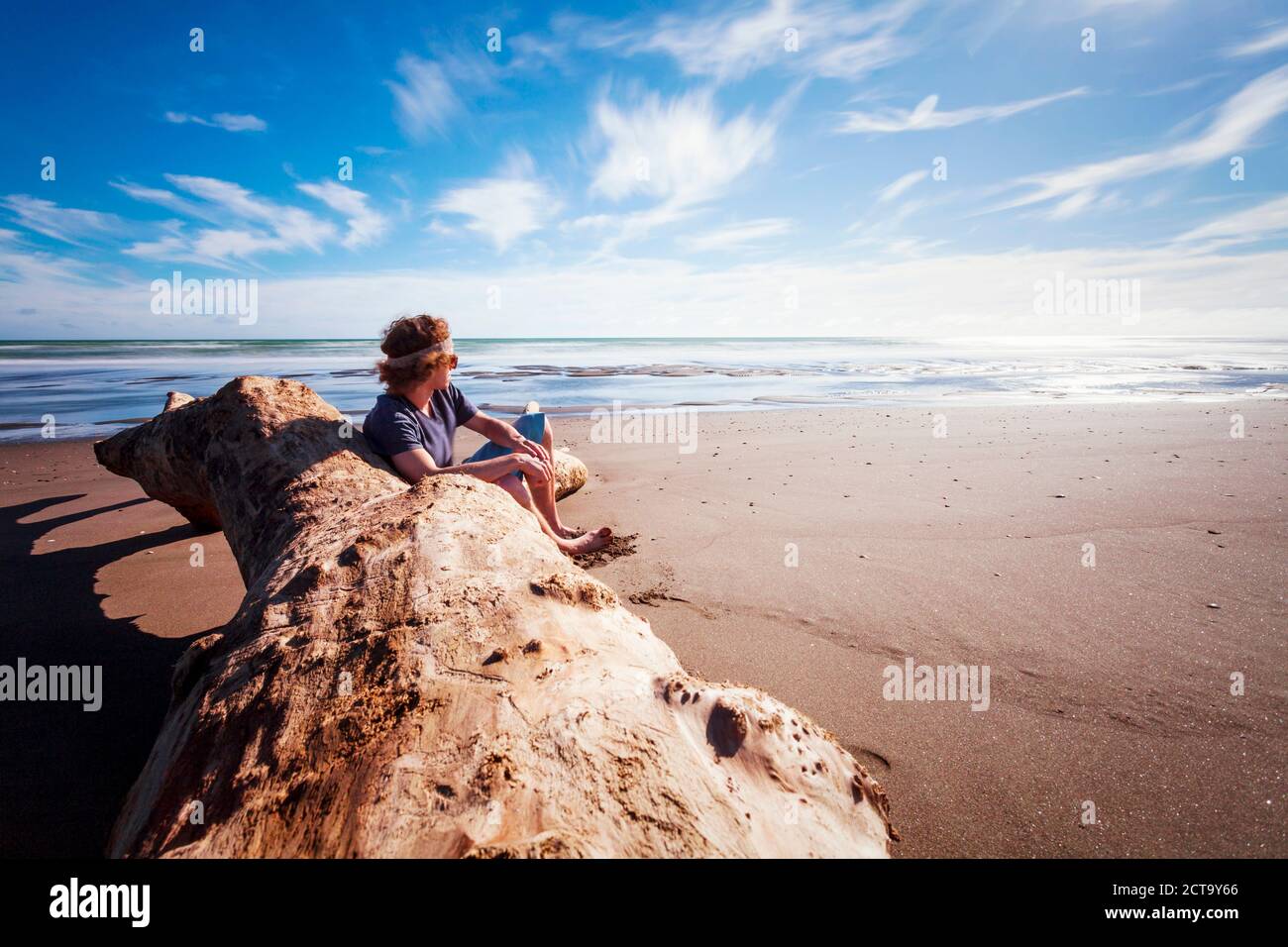 New Zealand, Wanganui beach, Young man sitting on beach Stock Photo - Alamy