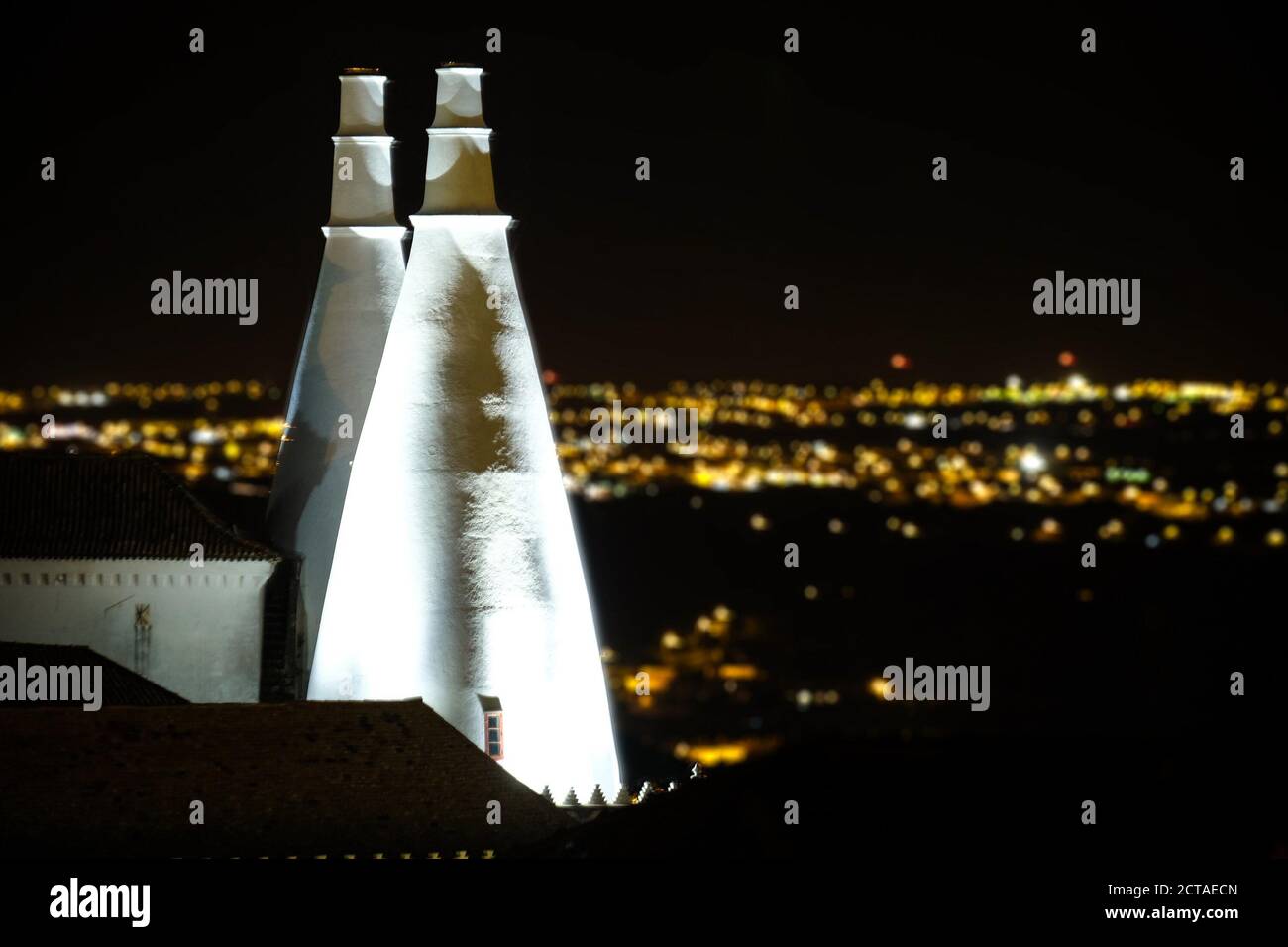 Chimneys of the Sintra Palace at night with the lights of the houses in ...