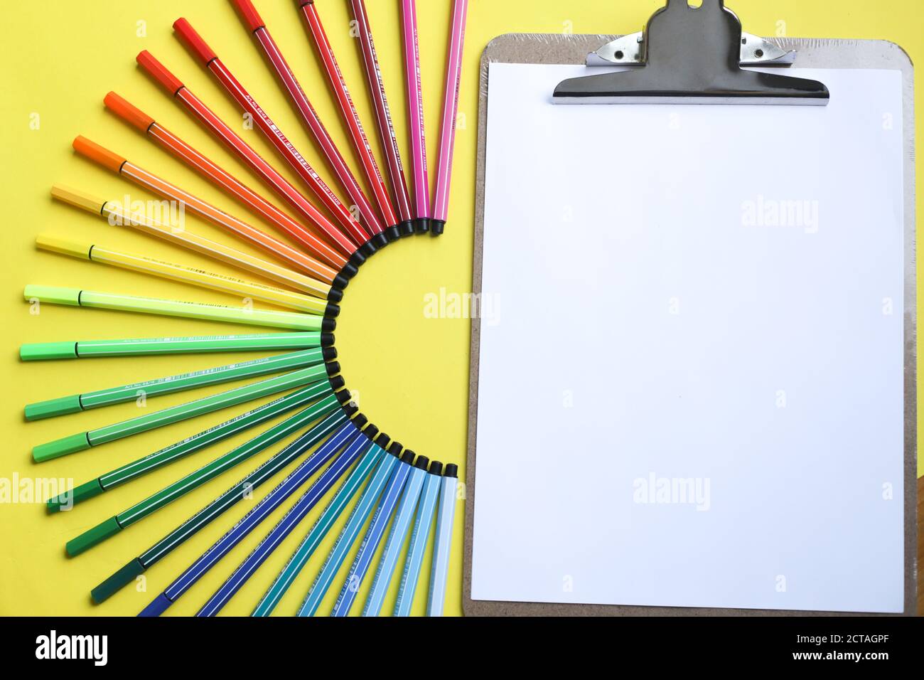 Shot of a drawing board with colored pencils on a yellow background ...