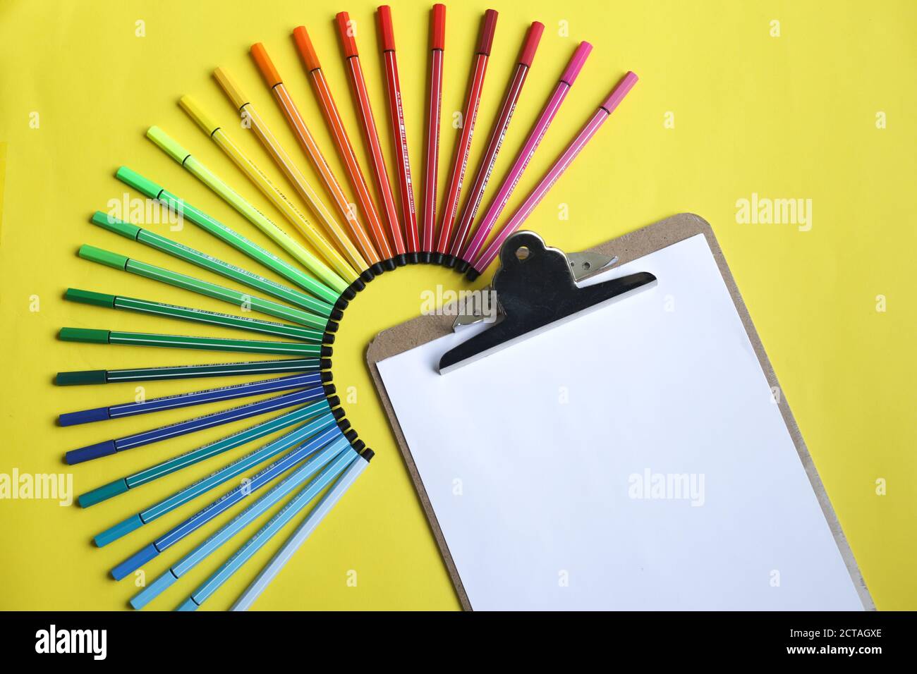 Shot of a drawing board with colored pencils on a yellow background ...