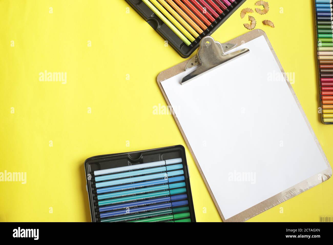 Shot of a drawing board with colored pencils on a yellow background ...