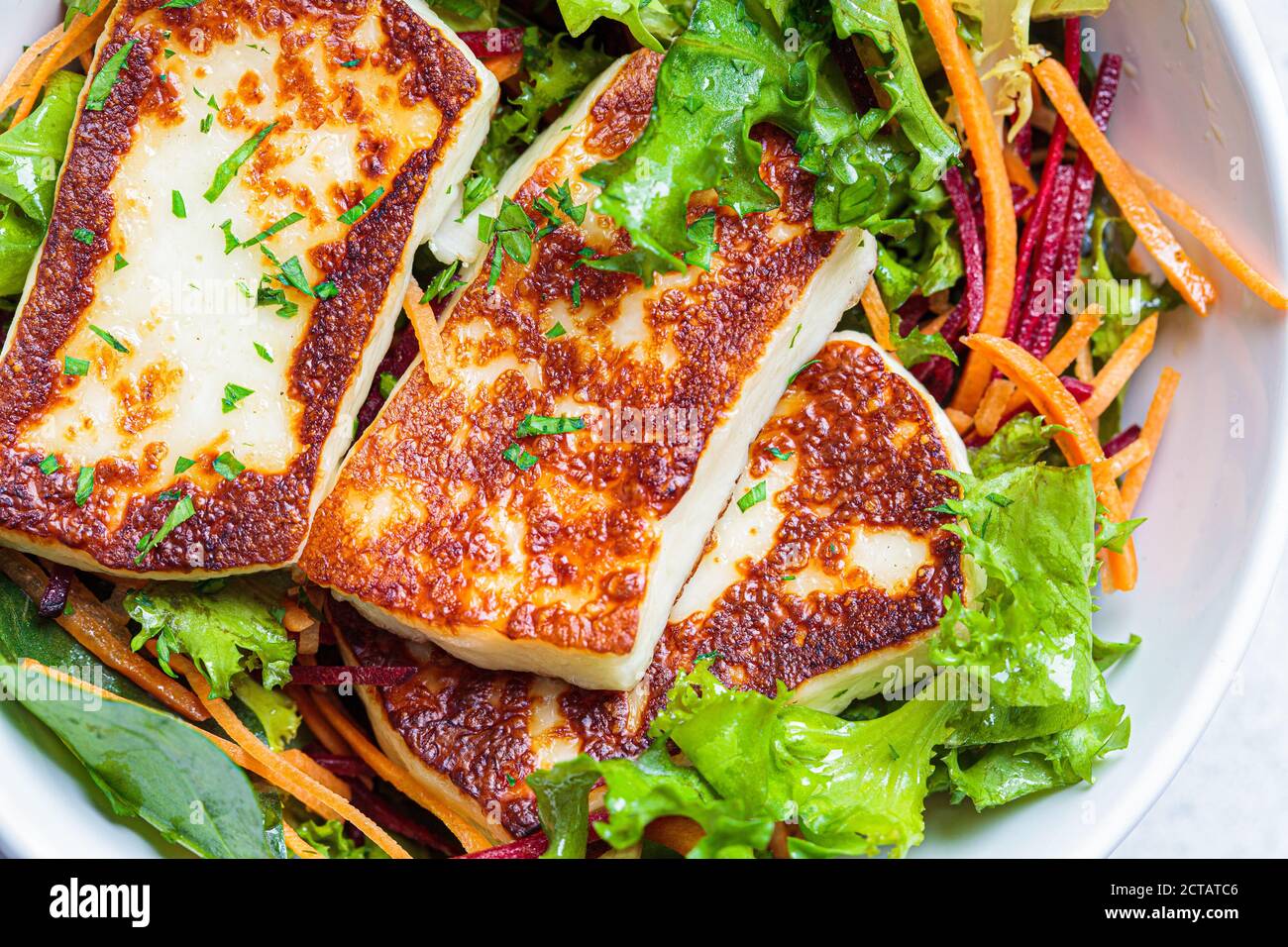 Green salad with grilled halloumi cheese, beets and carrots in a white ...