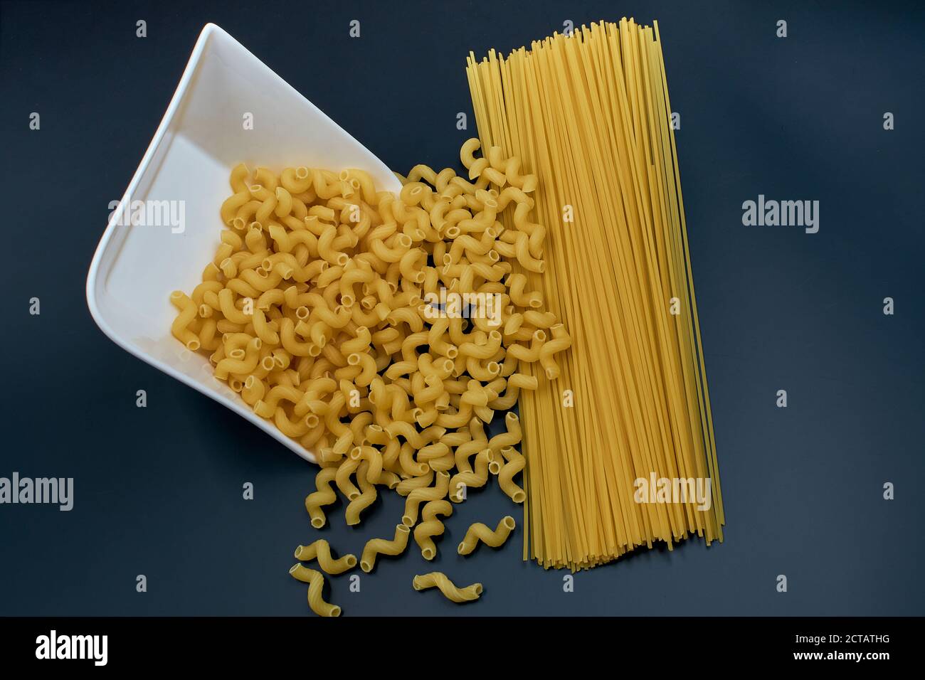 Small spring-shaped pasta is poured out of a white saucer. Spaghetti ...