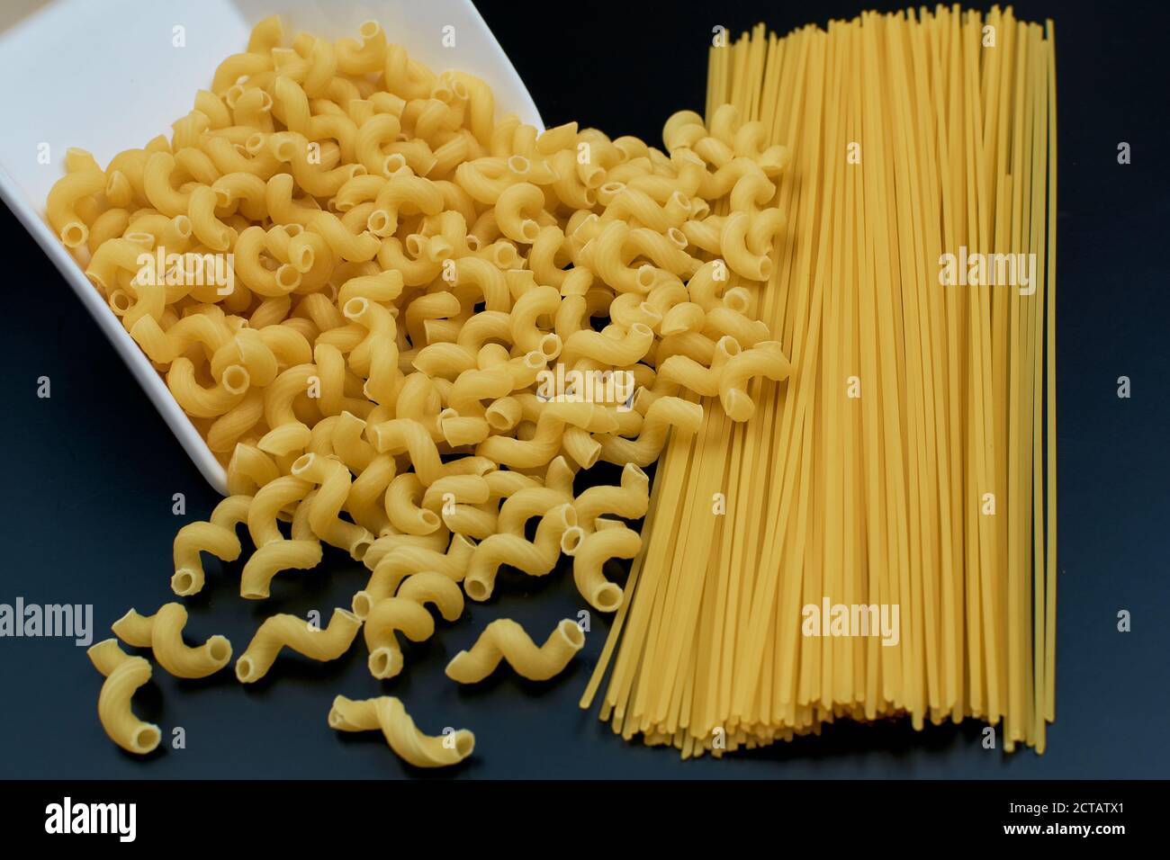 Small spring-shaped pasta is poured out of a white saucer. Spaghetti ...