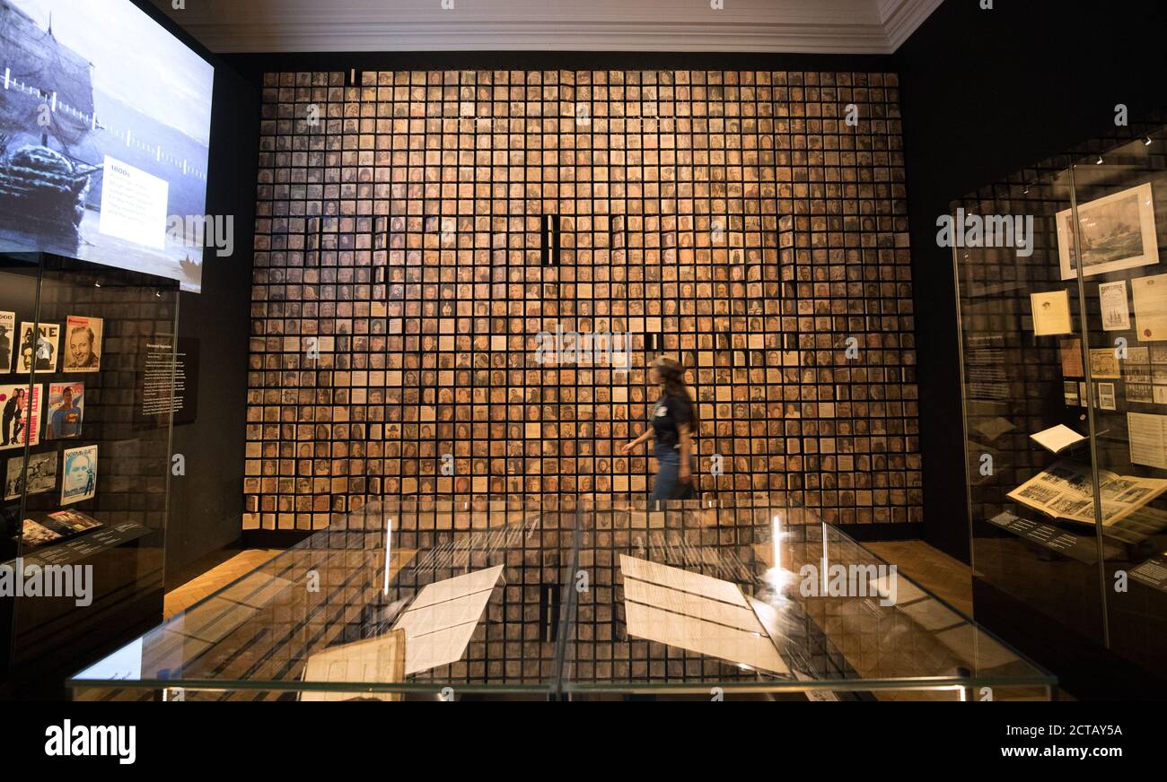 A staff member walks past a wall of faces of descendants related to the ...