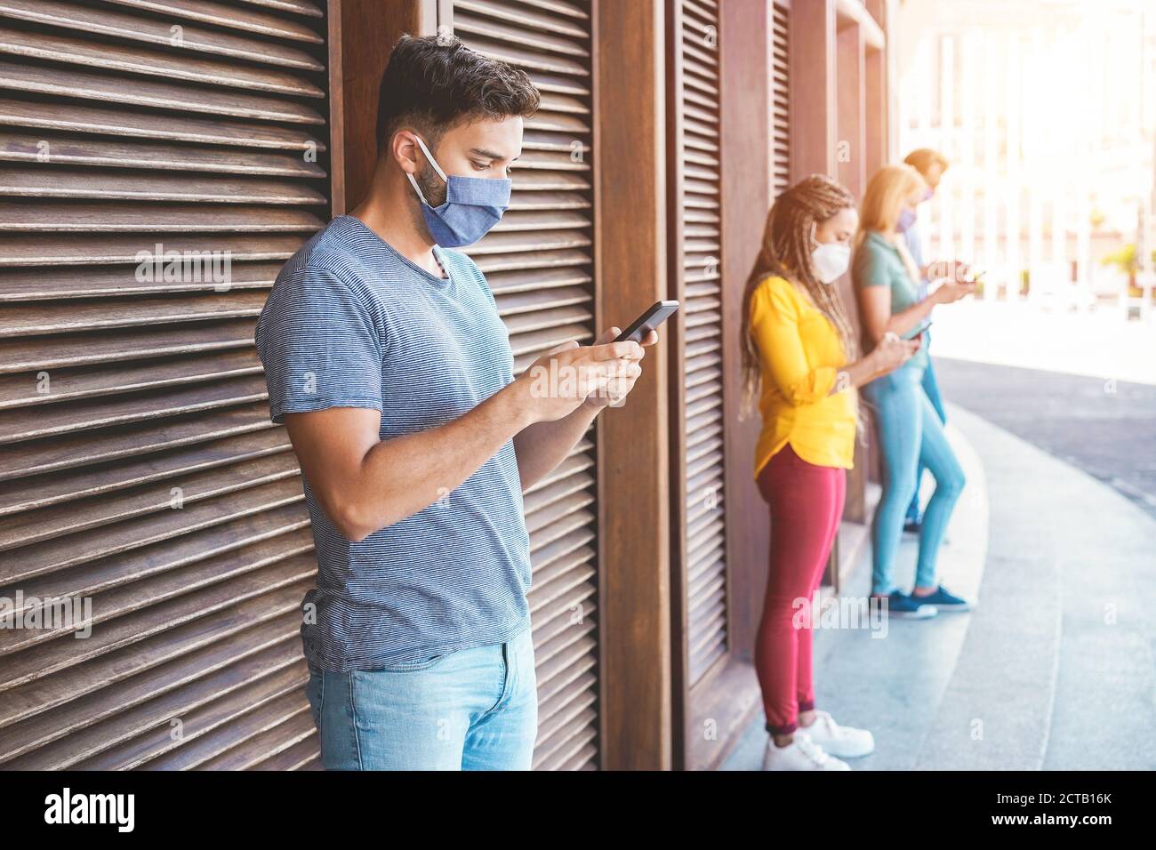 Young people wearing face safety masks using smart mobile phones while ...