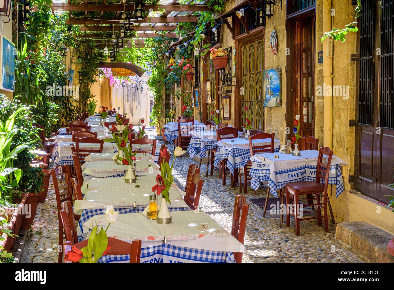 Tables and chairs under shade at a Greek taverna in the back streets of ...